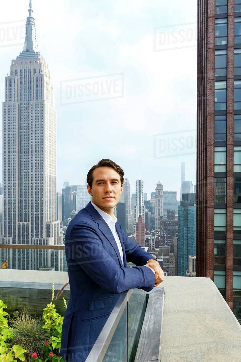 Portrait of serious Caucasian businessman leaning on urban rooftop ...