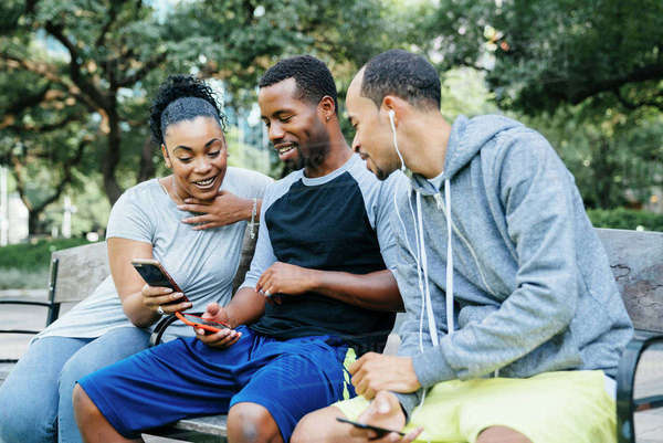 Black friends sitting on bench texting on cell phones - Royalty-free ...