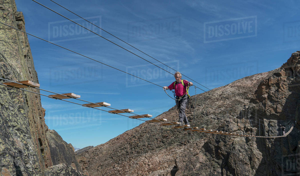 Caucasian man crossing rope bridge on mountain - Stock Photo - Dissolve