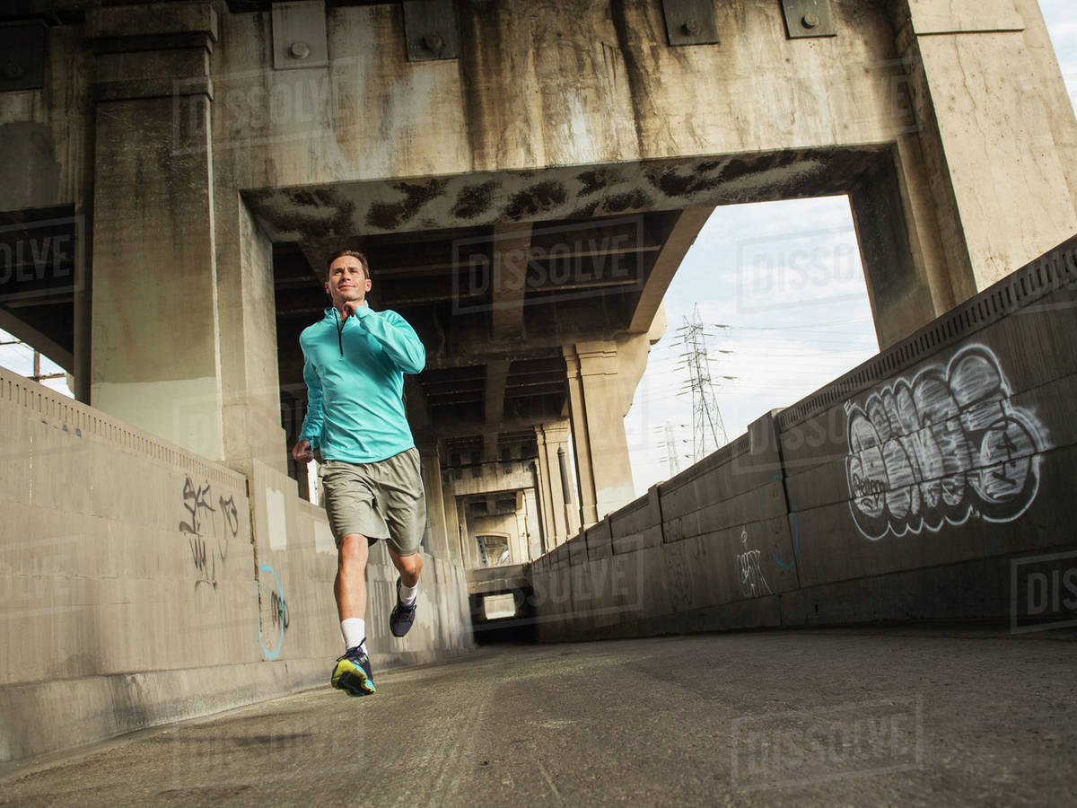 Caucasian man running in urban tunnel - Stock Photo - Dissolve