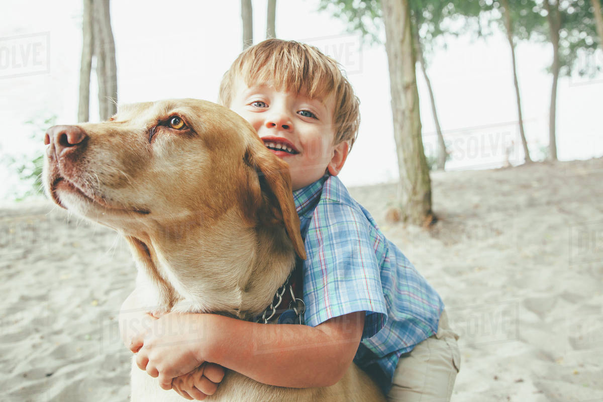 Boy hugging dog on wooded beach - Royalty-free Stock Photo | Dissolve