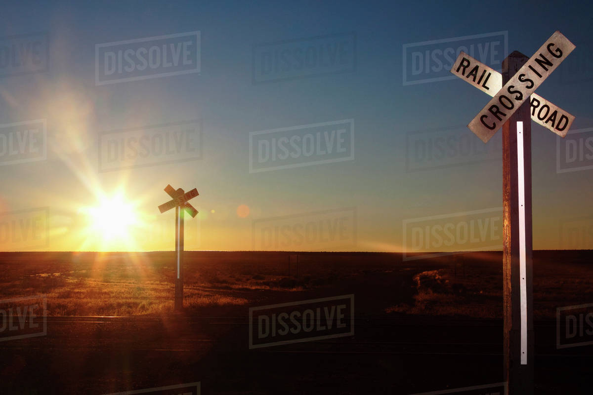 Railroad crossing sign on remote road at sunset - Stock Photo - Dissolve