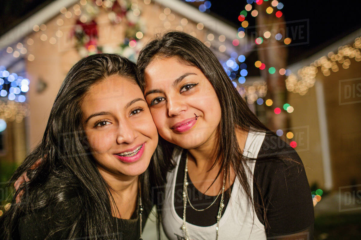 Hispanic sisters smiling outside house decorated with string lights ...