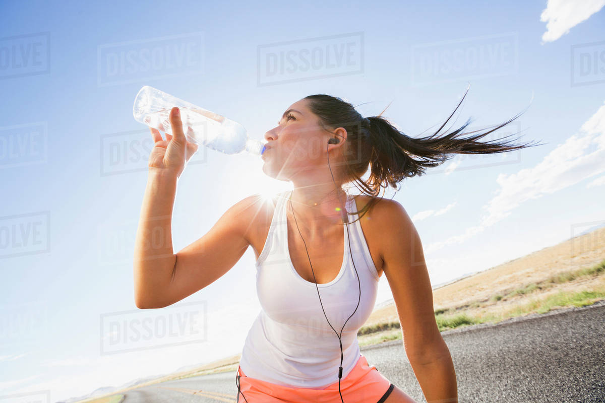 Caucasian runner drinking water bottle on remote road - Royalty-free ...