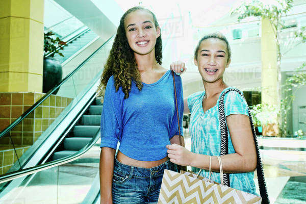 Mixed race teenage girls shopping near escalator at shopping mall ...