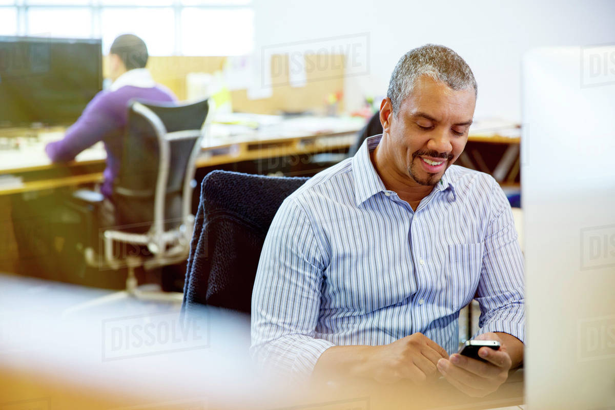 Businessman using cell phone at office desk - Stock Photo - Dissolve