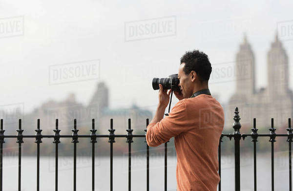 Mixed race man taking photograph on urban waterfront - Royalty-free ...