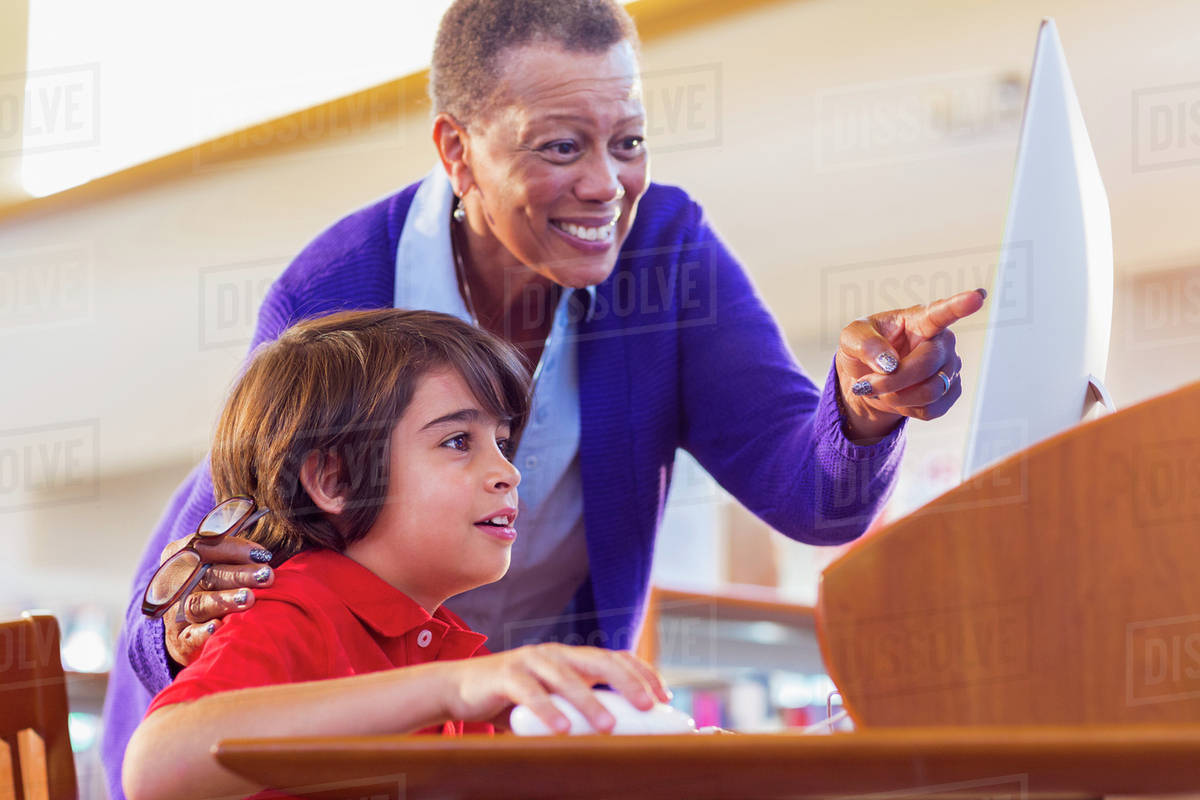 Teacher helping student use computer in library - Stock Photo - Dissolve