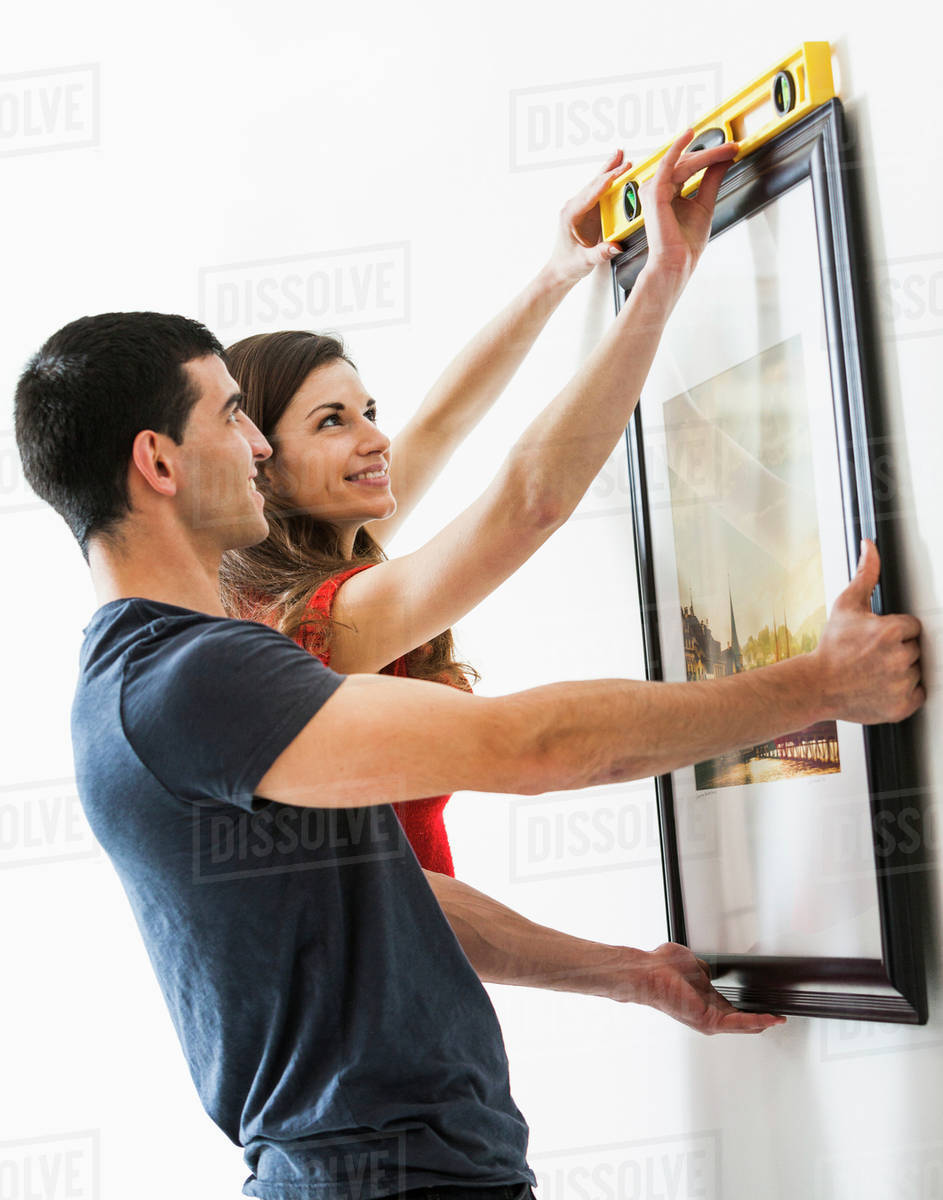 Couple measuring picture frame on wall - Stock Photo - Dissolve