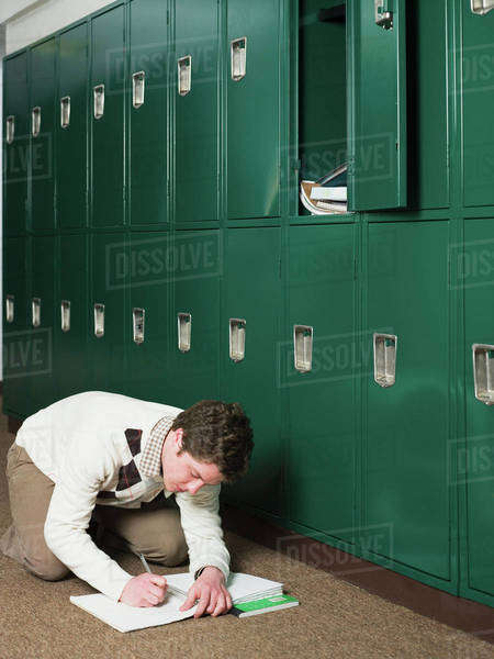 Student doing homework by locker in school hallway - Stock Photo - Dissolve