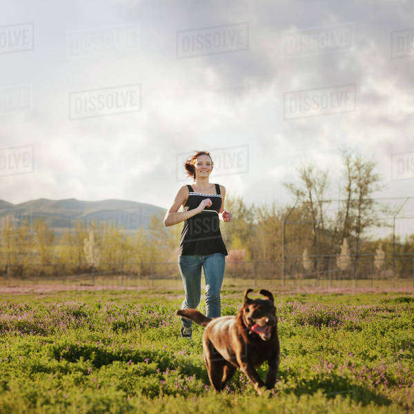 Caucasian woman running in field with dog - Royalty-free Stock Photo ...