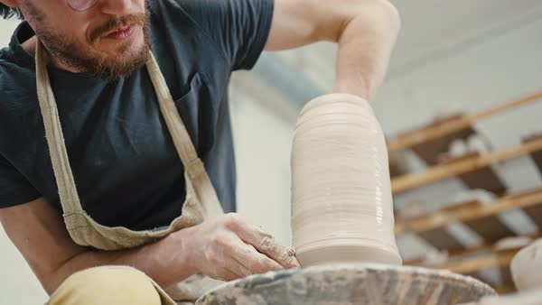 Close up shot of male potter artist sculpting ceramic vase on potter's ...