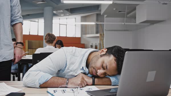 Indian employee fell asleep on work desk, his colleague is coming up to ...