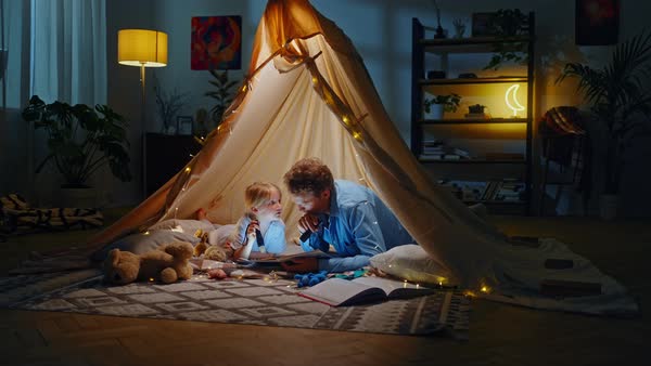Adorable little girl and her dad read bedtime story with a flashlight ...