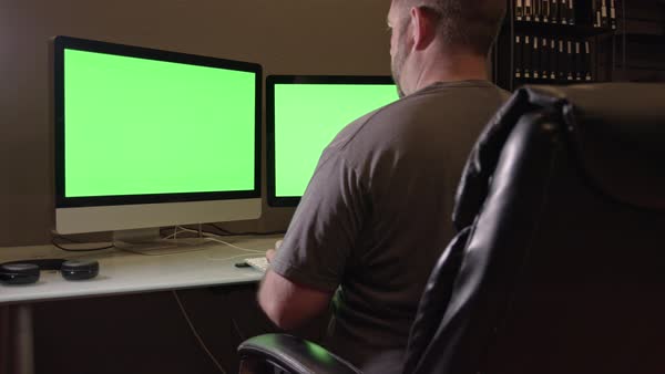 Man using dual screen computer with green screen at desk in office for ...