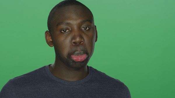 Young man makes funny faces, on a green screen studio background ...