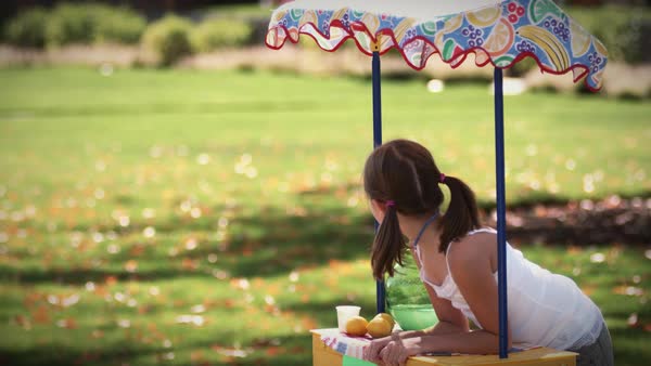 A young girl waits at her lemonade stand as three young girls run up ...