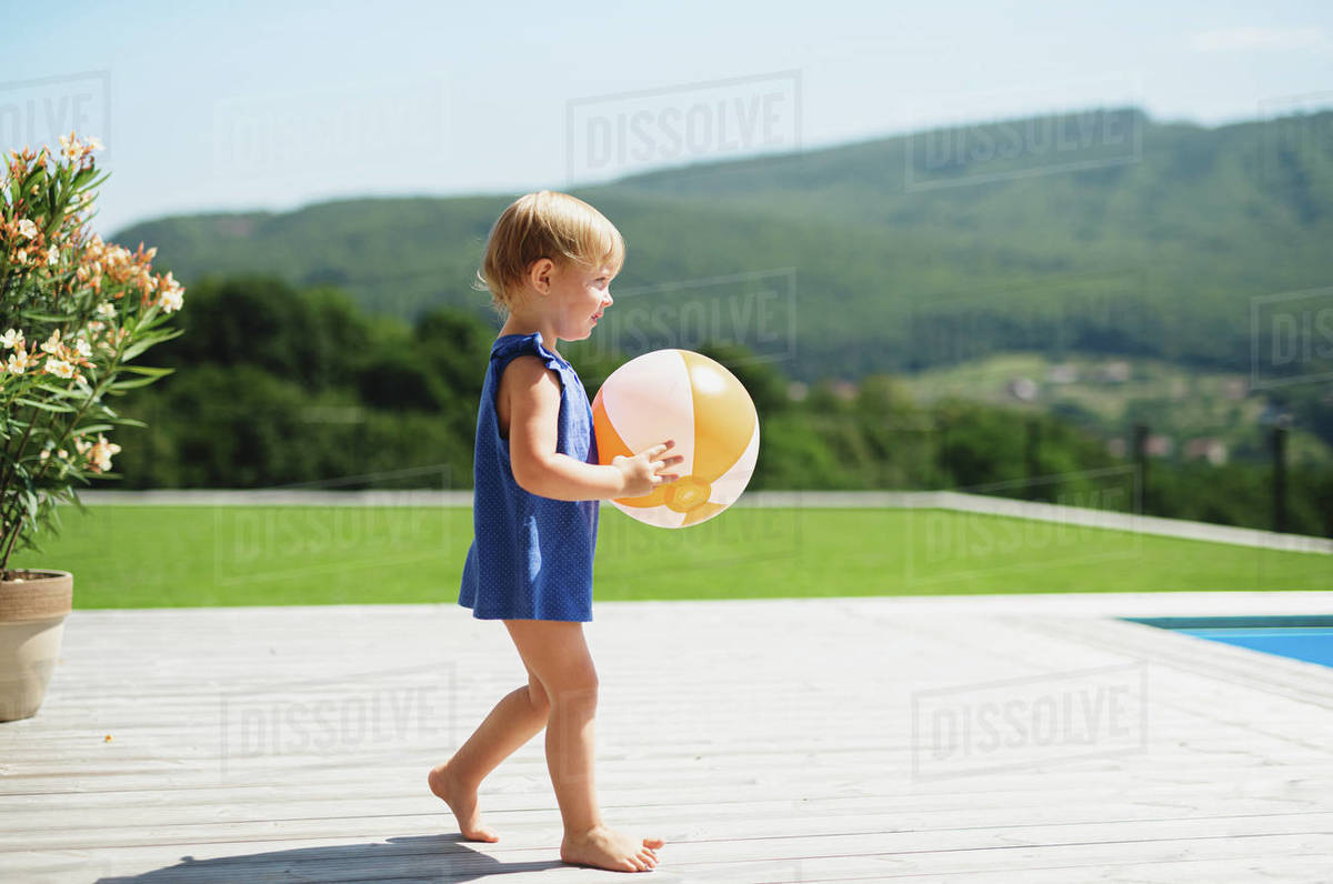 Side view portrait of small toddler girl with ball walking outdoors in ...
