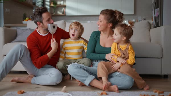 Little children playing with funny face masks with parents on sofa at ...