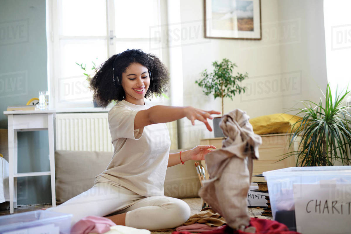 Happy young woman sorting clothes indoors at home, charity donation ...