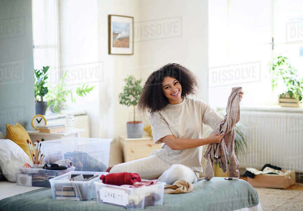 Happy young woman sorting clothing indoors at home, charity donation ...