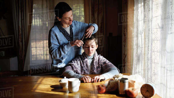 Portrait of sad poor woman cutting daughter's hair indoors at home ...