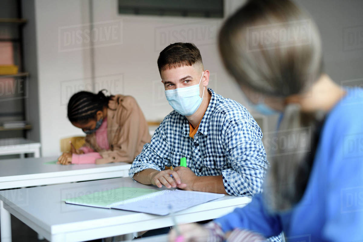 Portrait of young students with face masks at desks at college or ...