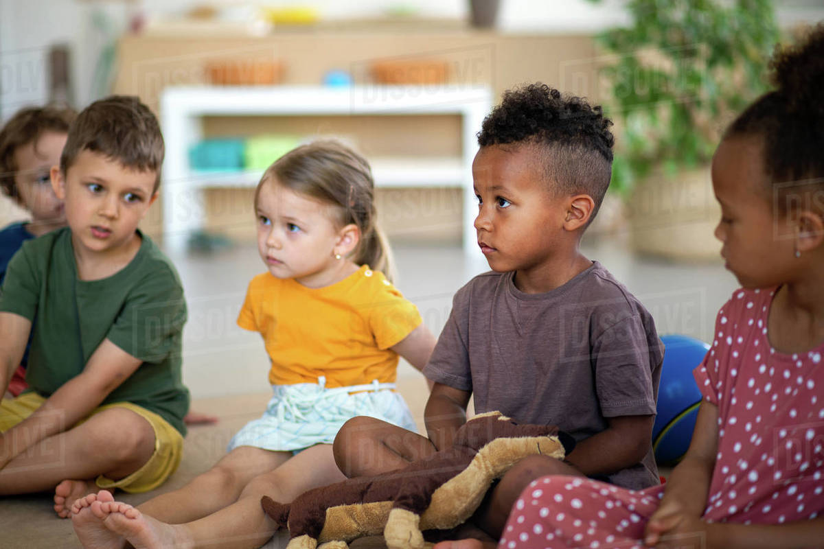 A group of small nursery school children sitting on floor indoors in ...