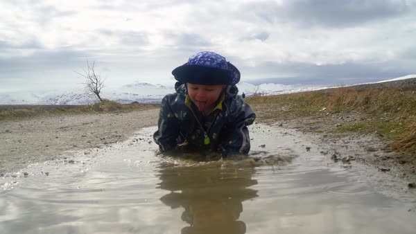 Cute baby sticking out tongue and crawling in dirty puddle on puddle ...