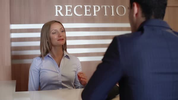 Close-up of stunning receptionist greeting hotel guest, checking his ...