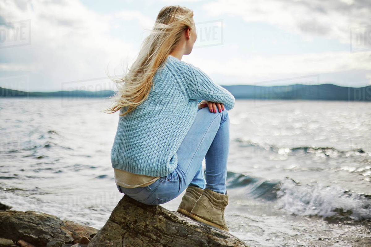 Rear view of young woman sitting on seaside at beach - Royalty-free ...