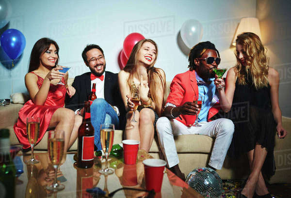 Happy friends sitting on a couch at a party with drinks - Royalty-free ...