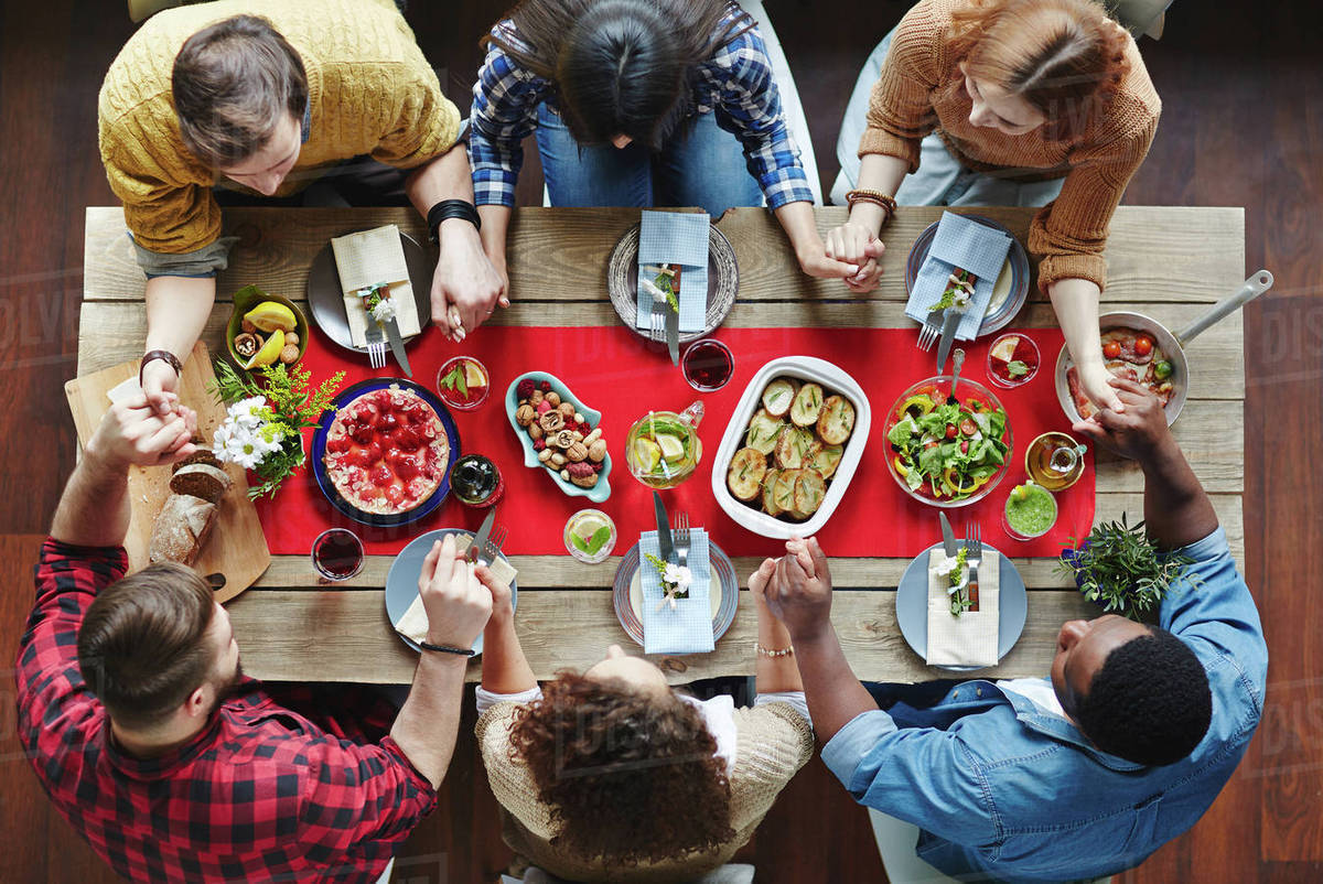 Friends sitting at dinner table holding hands - Royalty-free Stock ...