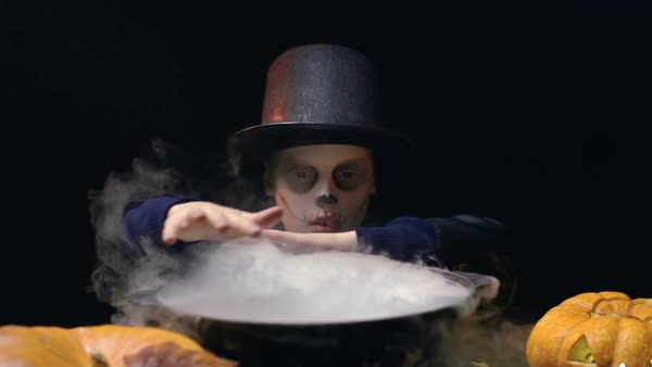Close up of little boy in skeleton disguise conjuring over evaporating ...