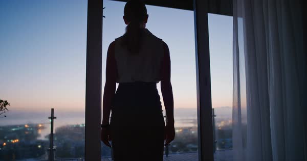 Young woman looking out window enjoying view of city at night ...