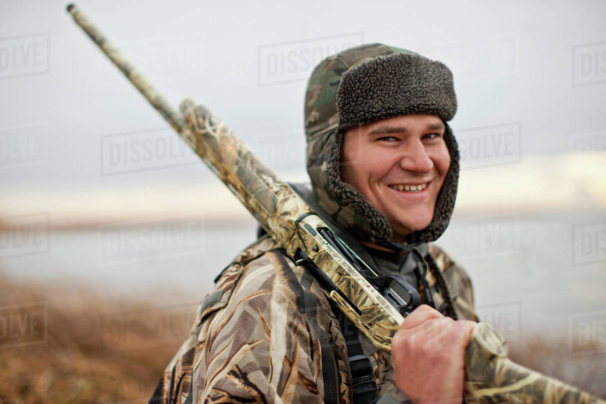 Portrait of a smiling duck hunter holding a shotgun while hunting ...