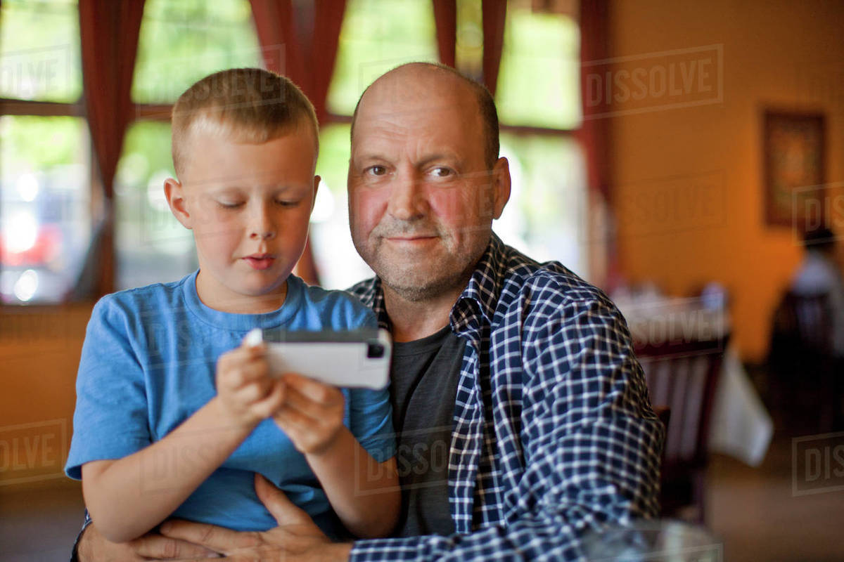 Portrait of a father with an arm around his son who is looking at a ...