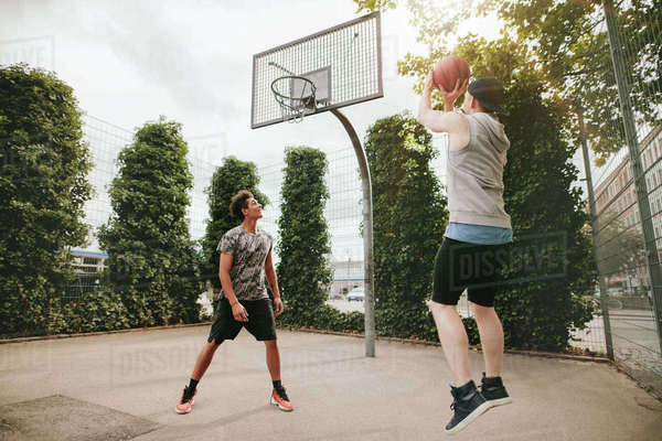 Young man taking jump shot with friend on basketball court. Streetball ...