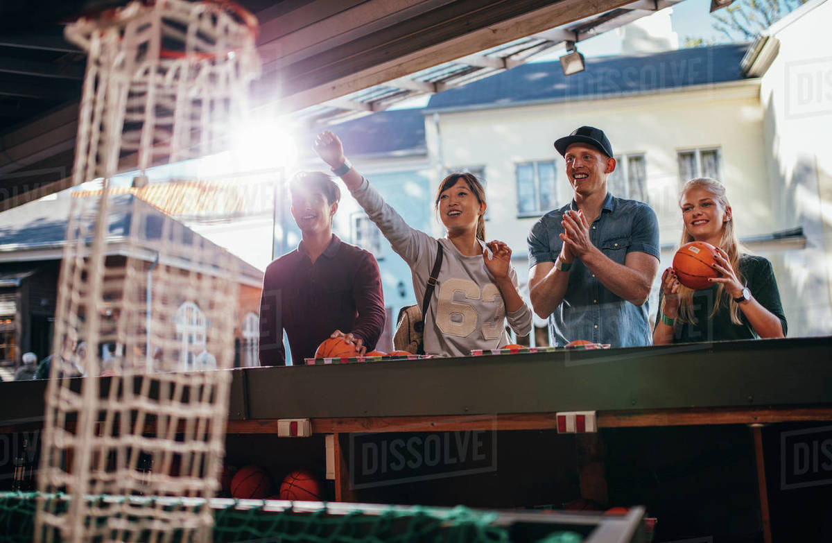 Happy young friends shooting hoops at amusement park and having fun ...