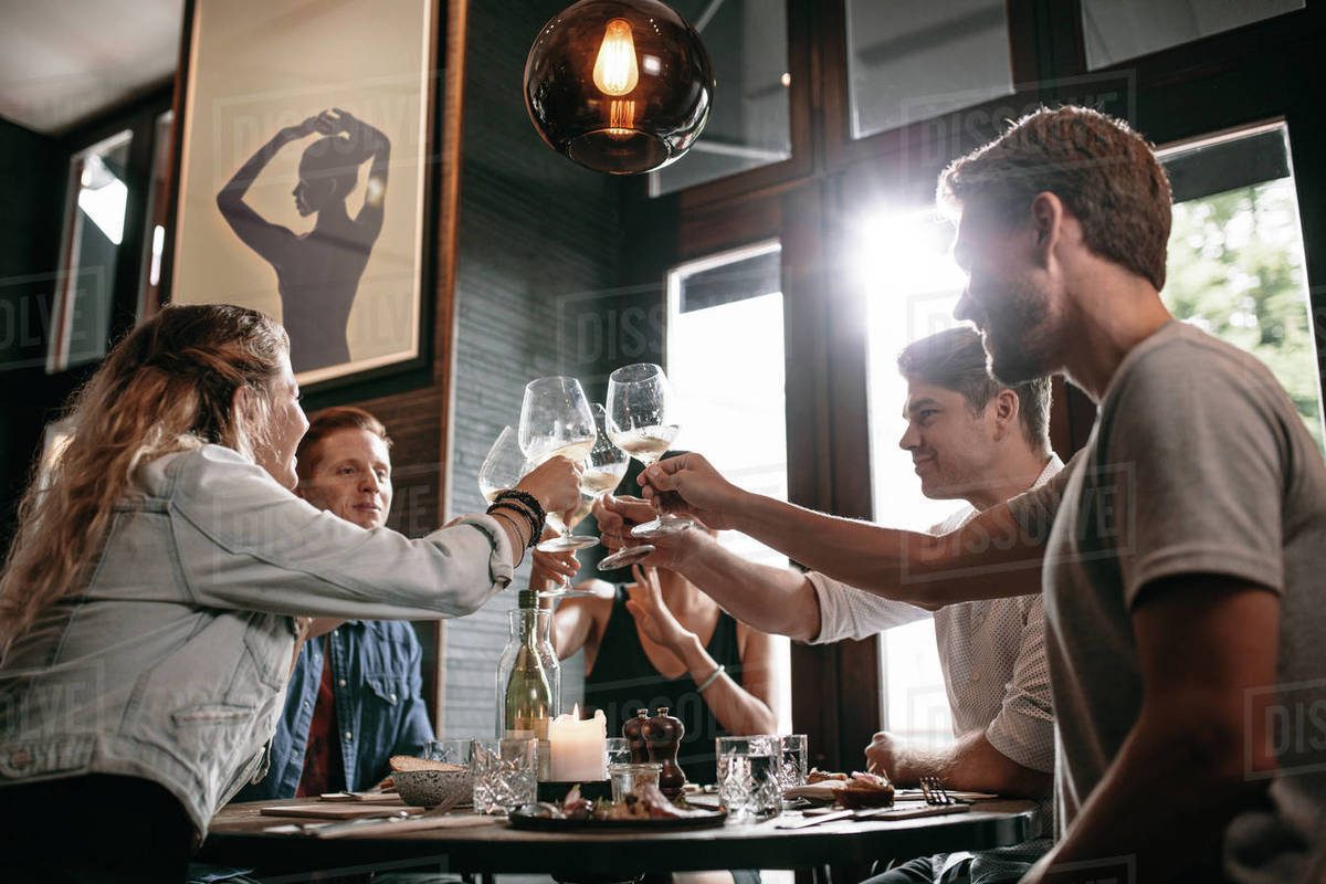 Young man and woman sitting at table and toasting drinks at restaurant ...