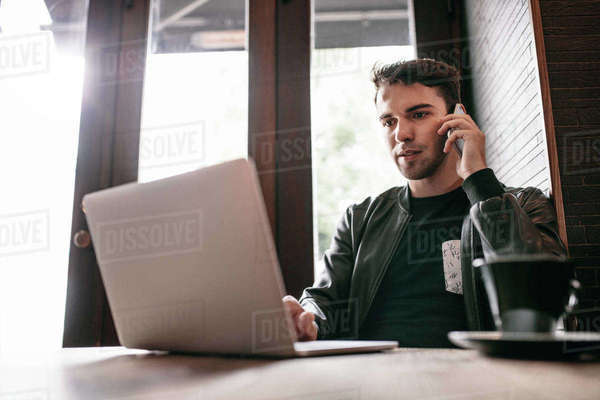 Indoor shot of young man sitting at a cafe table using laptop and ...