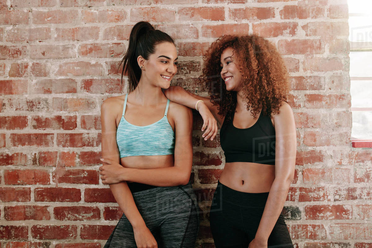 Portrait of two fitness females in gym relaxing and talking after ...