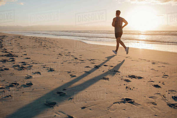 Shot of fit man running along the sea shore in morning. Healthy male ...