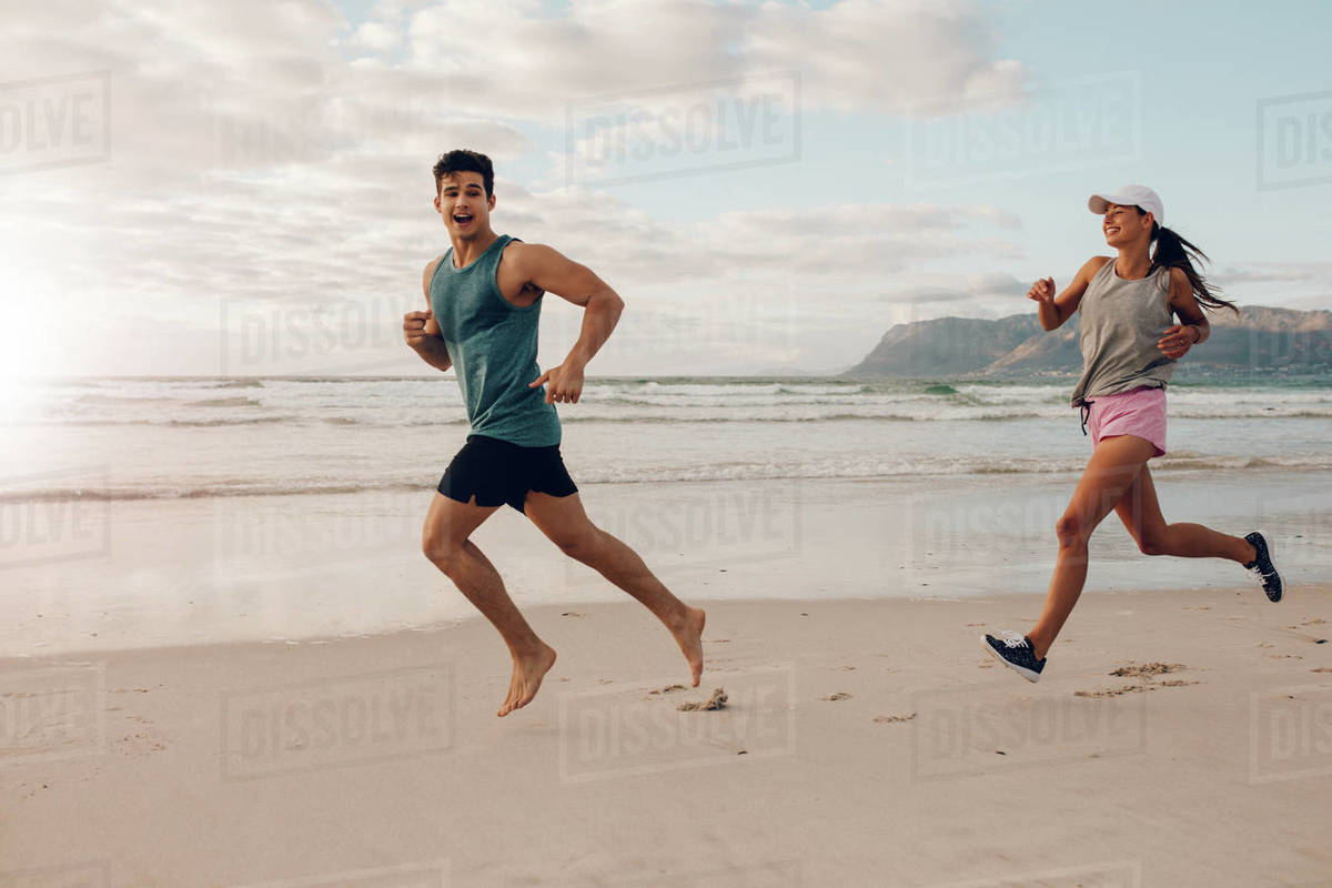 Full length shot of fit young man and woman running on the beach. Happy ...