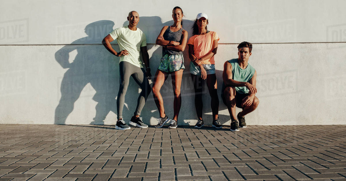 Full length shot mixed race friends posing by a wall. Fitness group ...