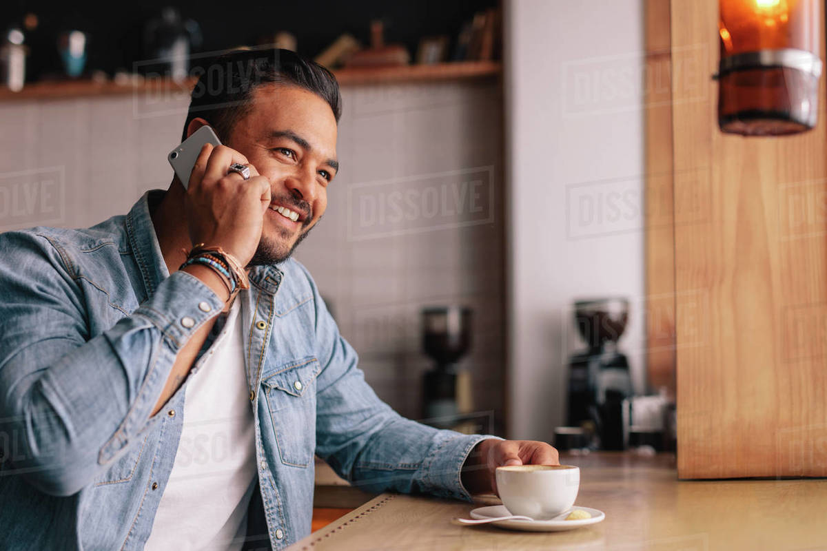 Indoor shot of handsome young man in coffee shop talking on mobile ...
