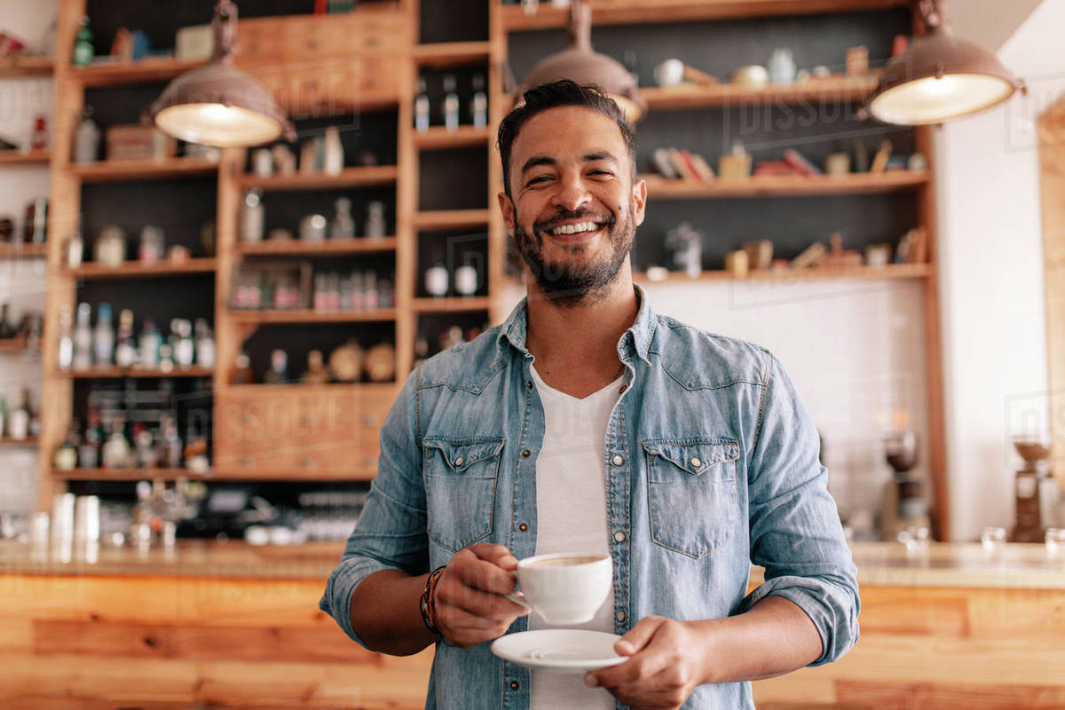 Portrait of handsome young man standing in a cafe with a cup of coffee ...
