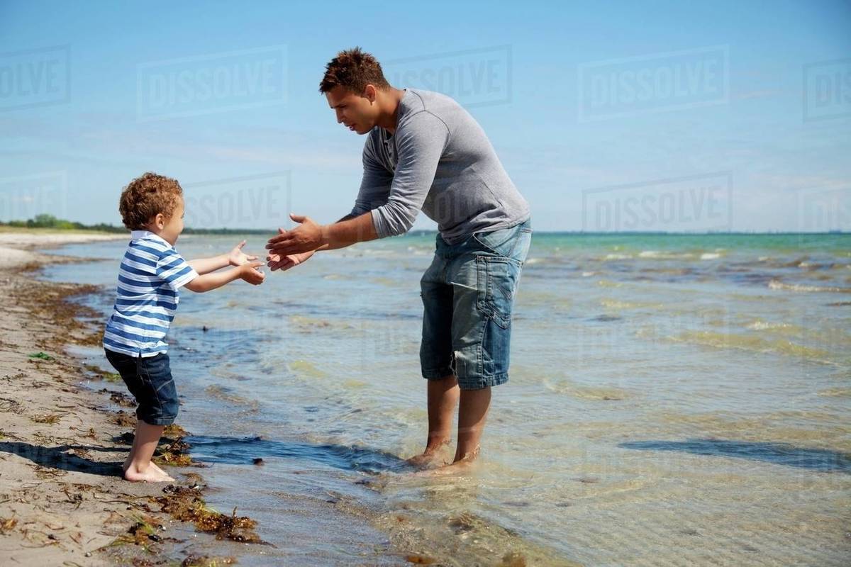 Cute boy takes little steps towards his father to dip in the sea ...