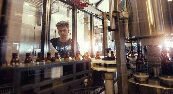 Factory worker looking at conveyor with beer beverage bottles moving ...