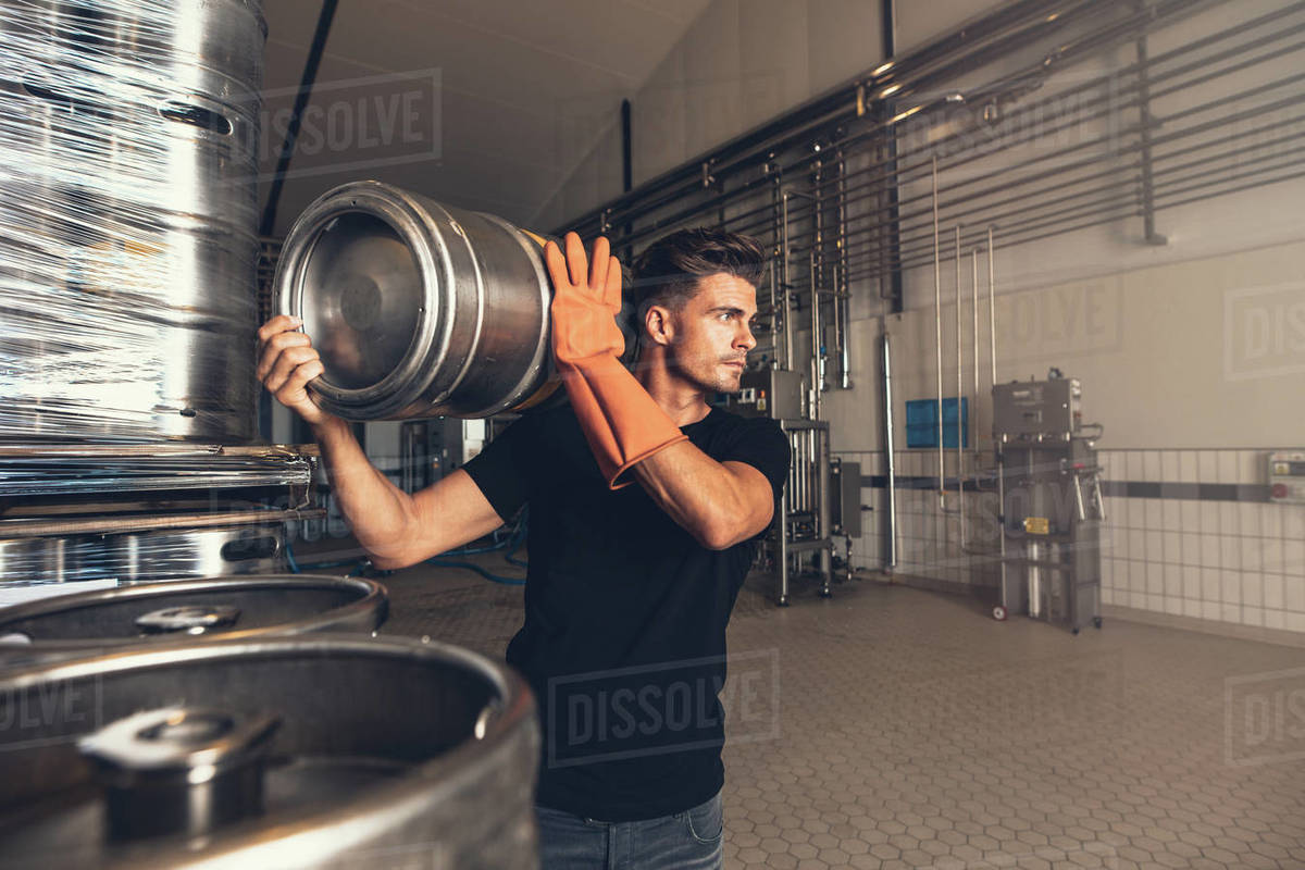 Brewer with large metal container at brewery factory. Young man working ...